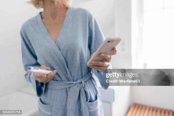 Closeup Of Woman With Cell Phone And Toothbrush In Bathroom High Res