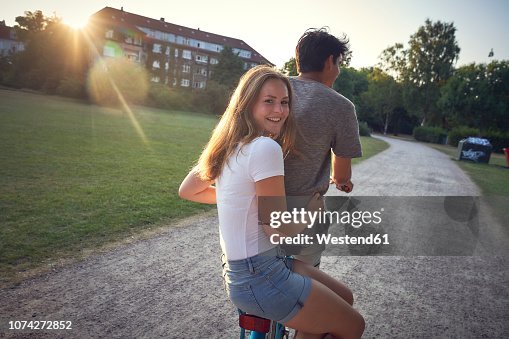 Young Couple Riding Bicycle In Park Woman Sitting On Rack High Res