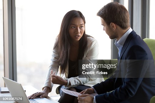 Asian Caucasian Colleagues Sitting On Couch Discussing Solve Business