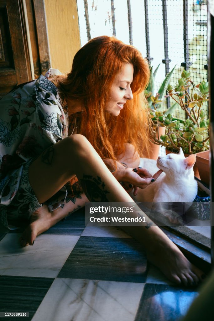 Redhaired Tattooed Woman Playing With Her Cat At Home High Res Stock