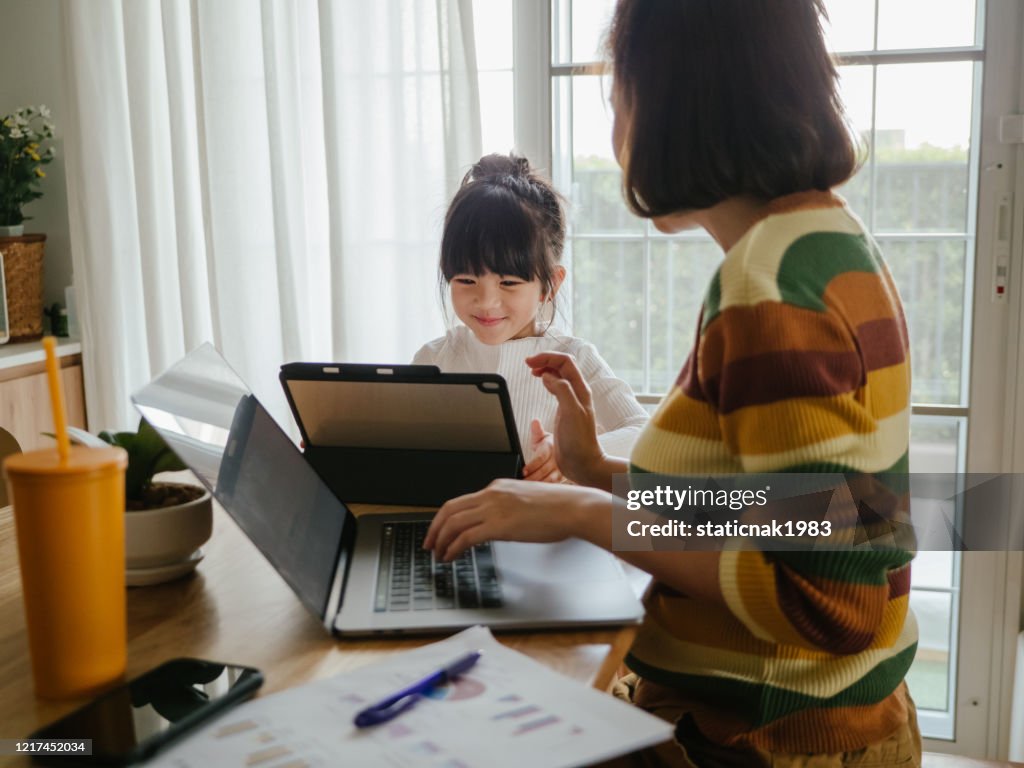 Mother Working On Laptop And Daughter Watching Cartoon On Tablet High