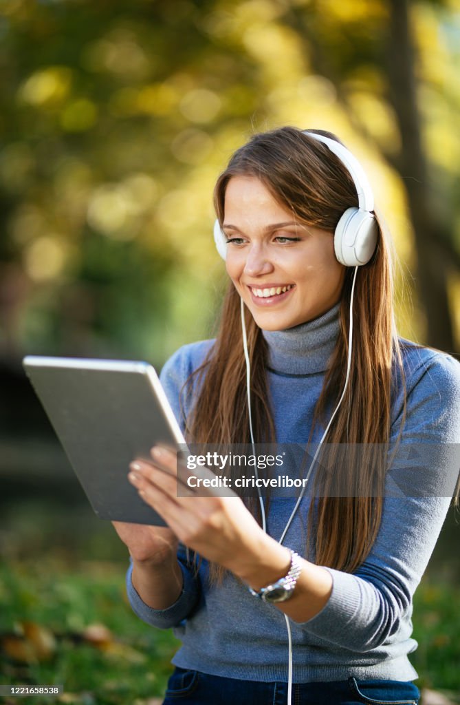 Smiling Young Woman Using Digital Tablet And Listening Music In Nature ... Smiling Young Woman Using Digital Tablet And Listening Music In Nature ...