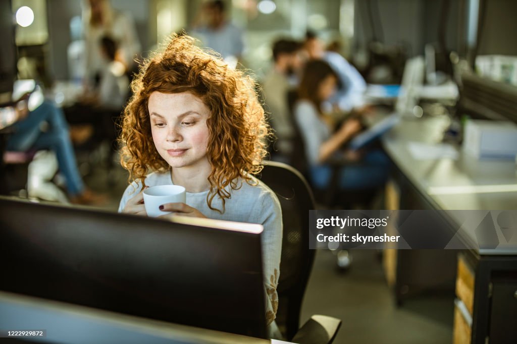 Female Redhead Programmer Drinking Coffee While Working On Desktop Pc ... Female Redhead Programmer Drinking Coffee While Working On Desktop Pc ...
