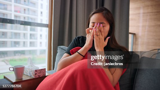 Sickly Young Woman Blowing Her Nose With A Tissue Staying On A Couch