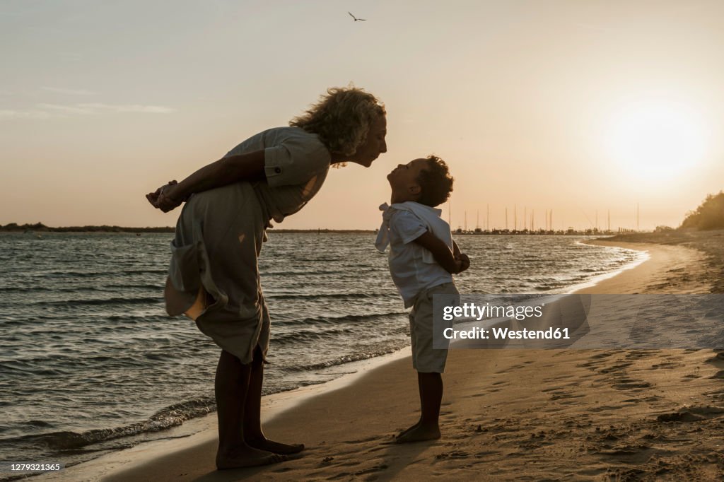 Grandson And Grandmother Doing Kissing Gesture At Beach During Sunset
