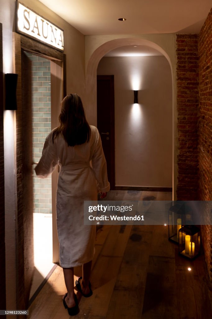 Young Female Customer Wearing Bathrobe Entering Sauna At Health Spa
