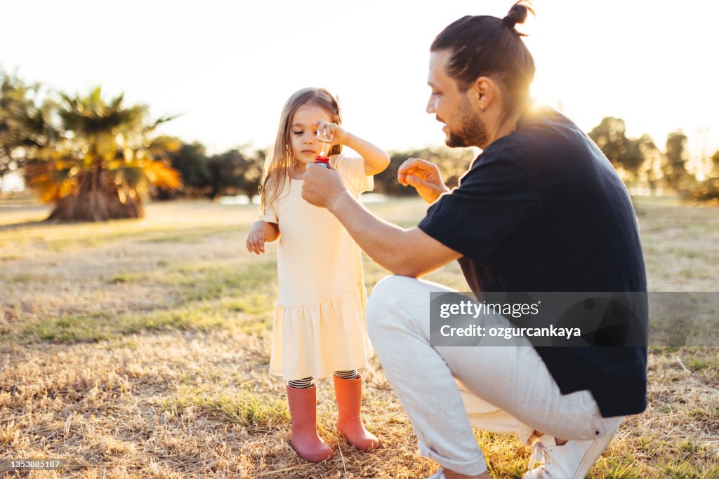 Father And Daughter Having Fun In Park With Soap Bubbles High Res Stock