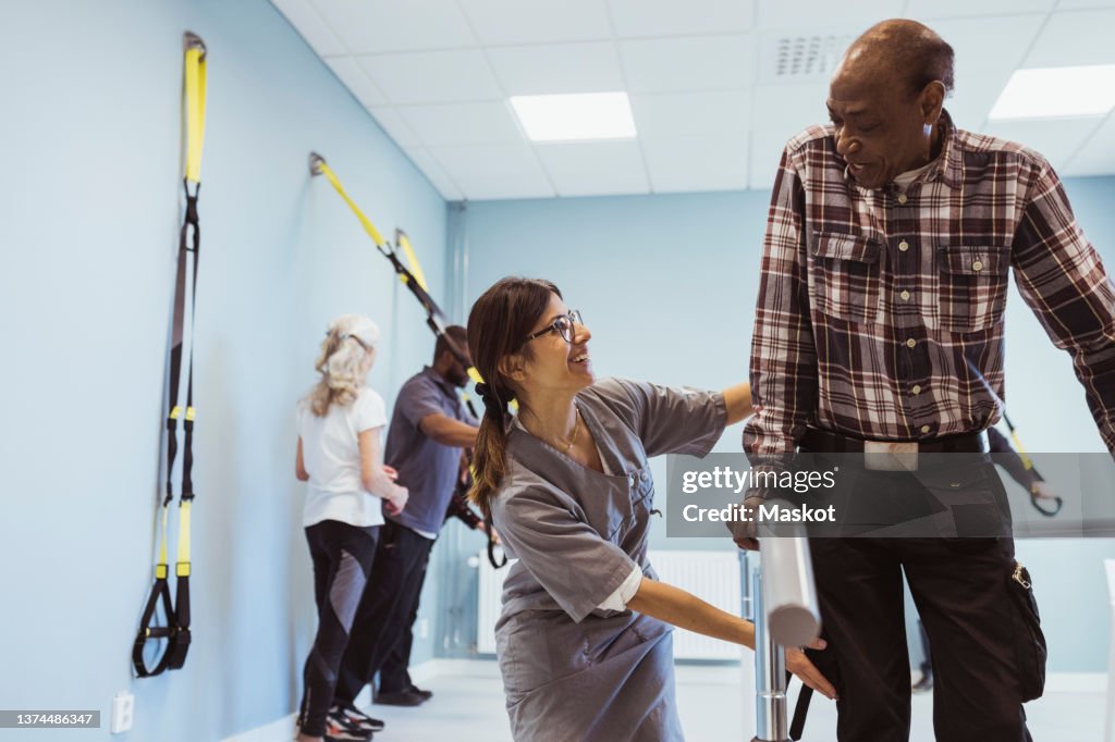 Smiling Female Caregiver Helping Senior Man To Walk At Nursing Home