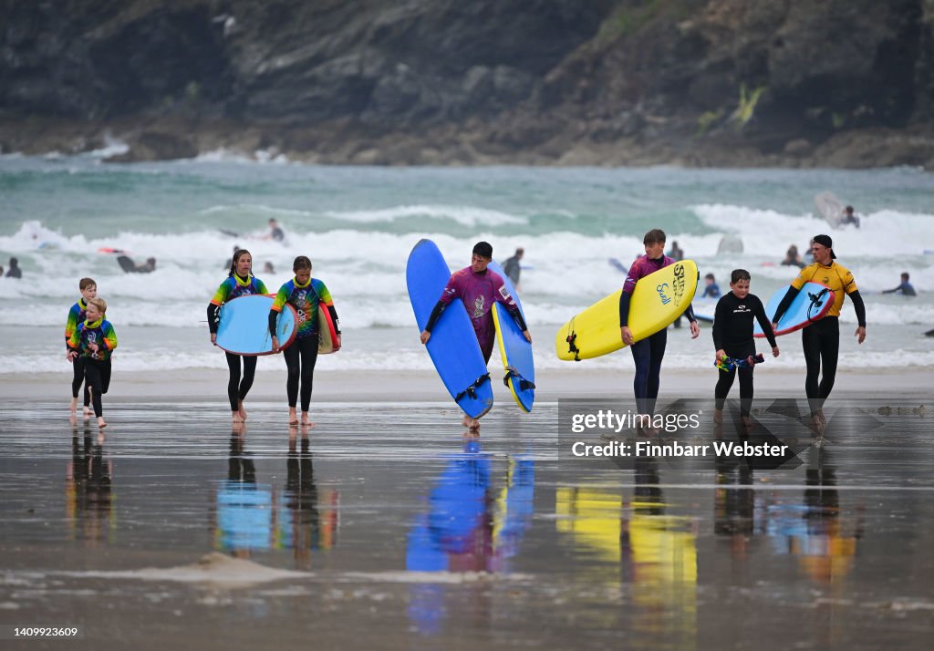 People Leave The Sea Carrying Their Surfboards At Polzeath Beach On