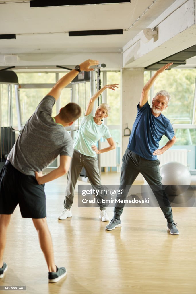Senior Couple Doing Stretching Exercises With Personal Trainer At The