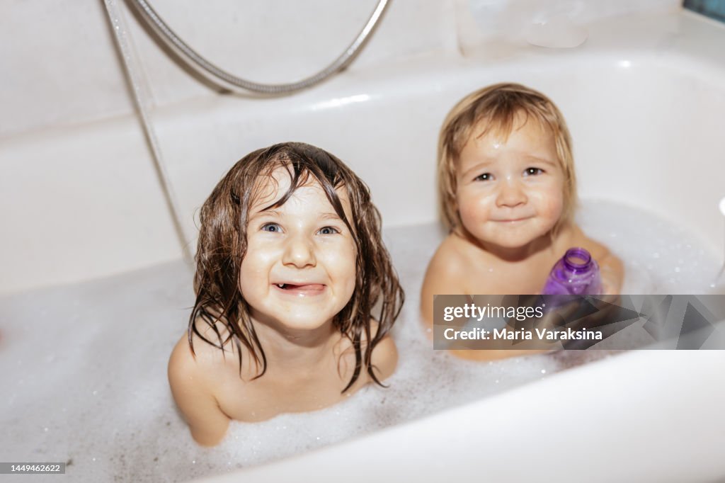 Two Small Sisters Sitting In A Bath With Foam And Toys High Res Stock