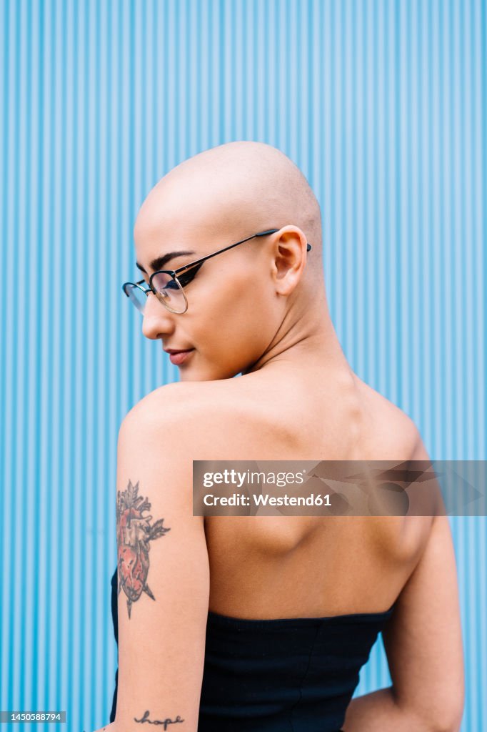 Woman With Shaved Head Wearing Eyeglasses In Front Of Blue Wall High