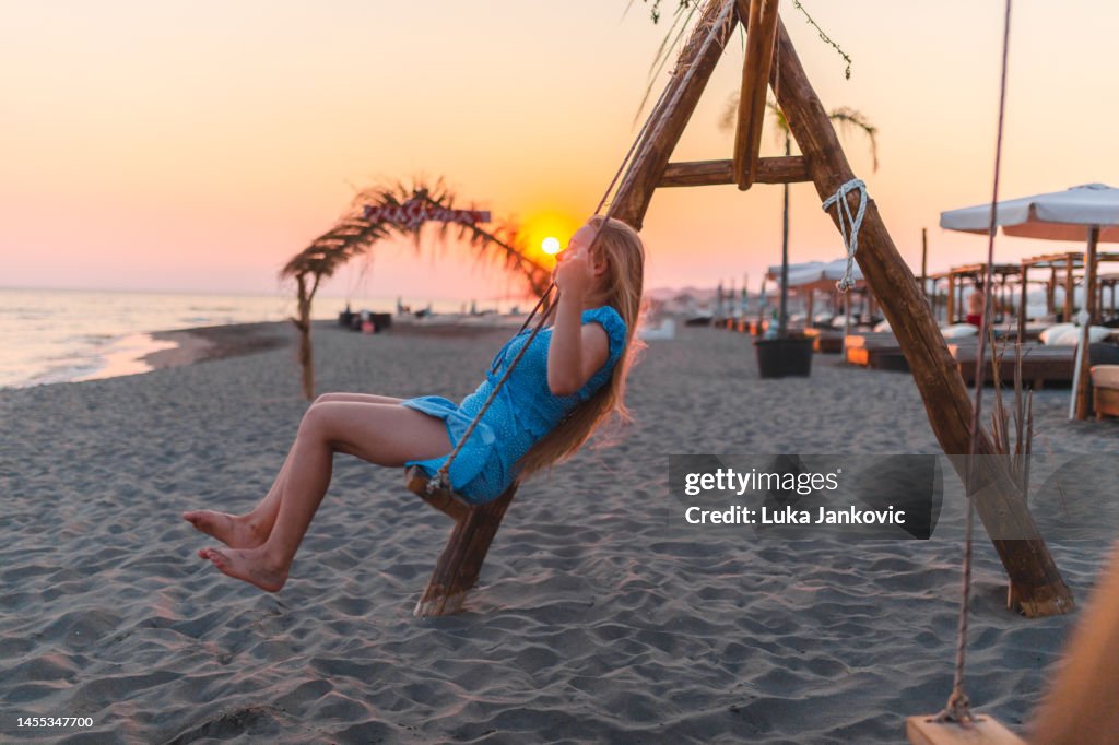 Beautiful Young Blonde Woman Swinging On The Beach By The Sea During