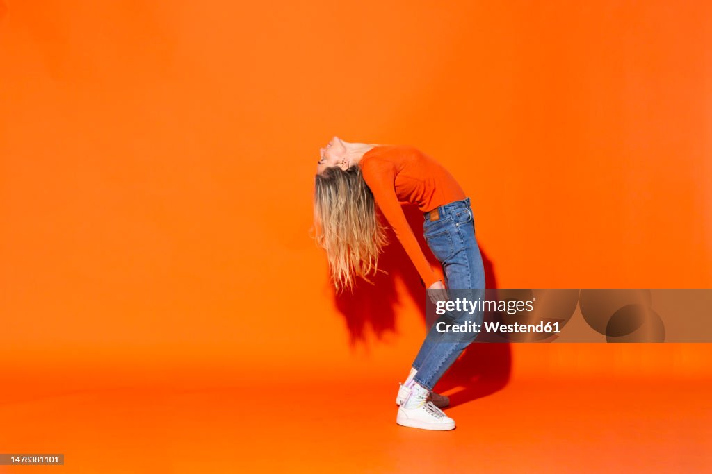 Woman Bending Over Backwards Against Orange Background Stock Foto