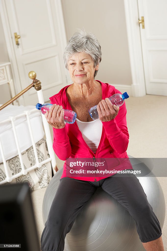 Senior Woman Exercising Whilst Watching Fitness Dvd On Televisio High