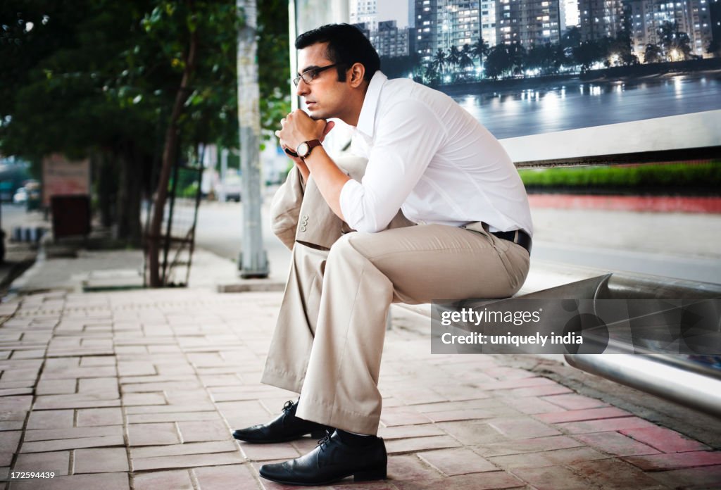 Businessman Sitting On A Bench At Bus Stop And Looking Thoughtful High