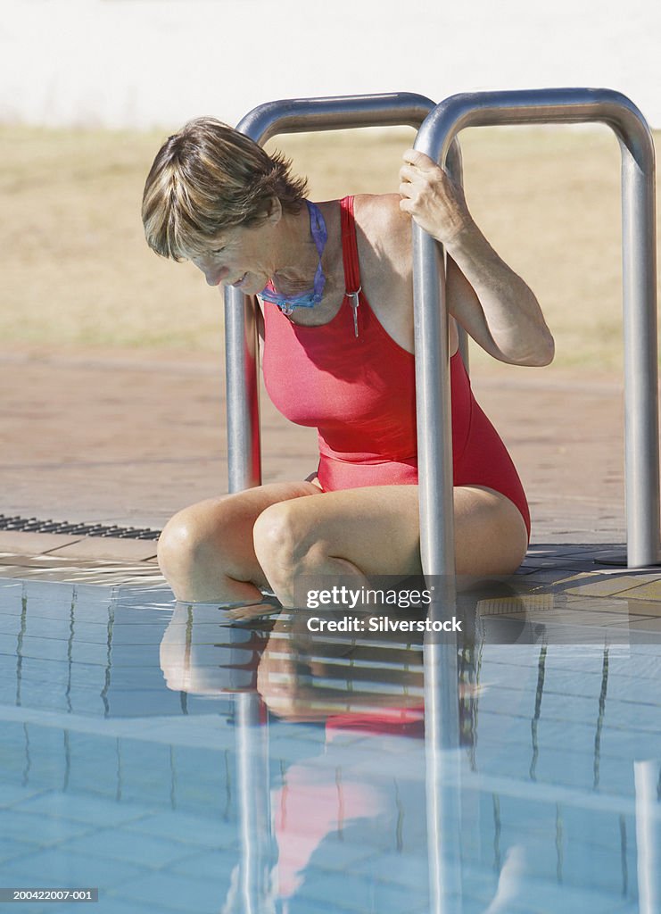 Mature Woman Sitting At Edge Of Swimming Pool Wearing Swimsuit High Res