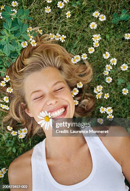 Young Woman Lying On Grass With Daisy In Mouth Smiling High Res Stock