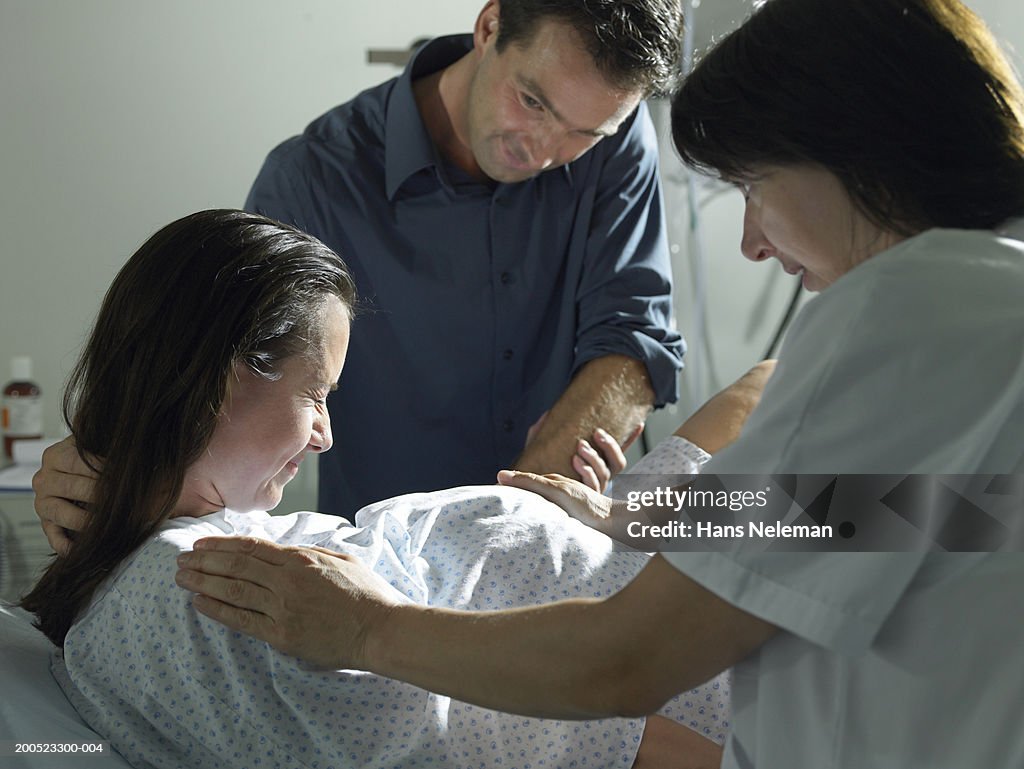 Midwife And Husband Supporting Pregnant Woman Giving Birth In Hospital
