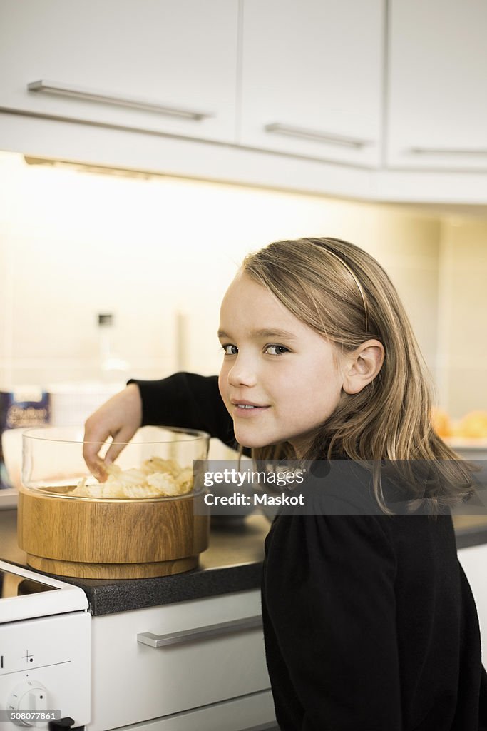Side View Portrait Of Girl Eating Potato Chips At Kitchen Counter High