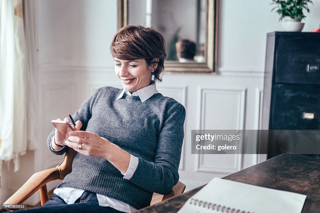 Beautiful Mid Aged French Woman With Smartphone In Home Office High Res