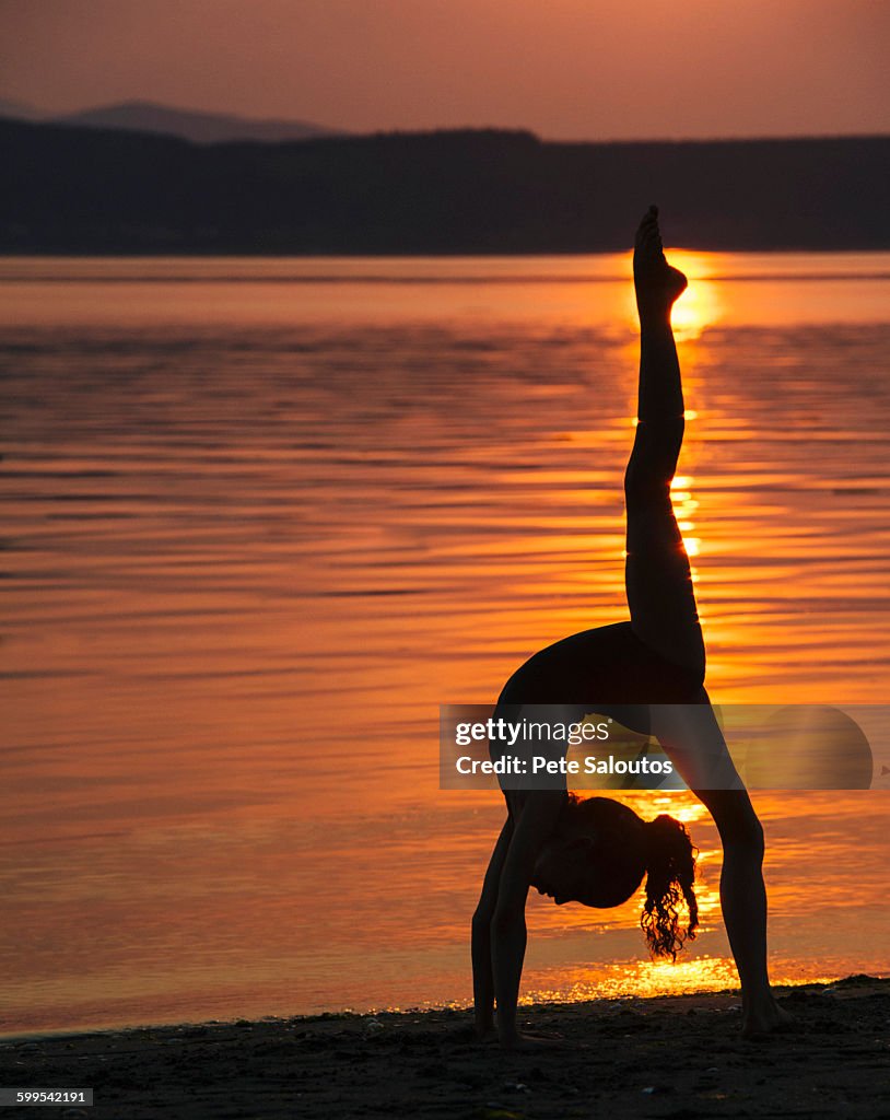 Side View Of Girl In Silhouette By Ocean At Sunset Bending Over
