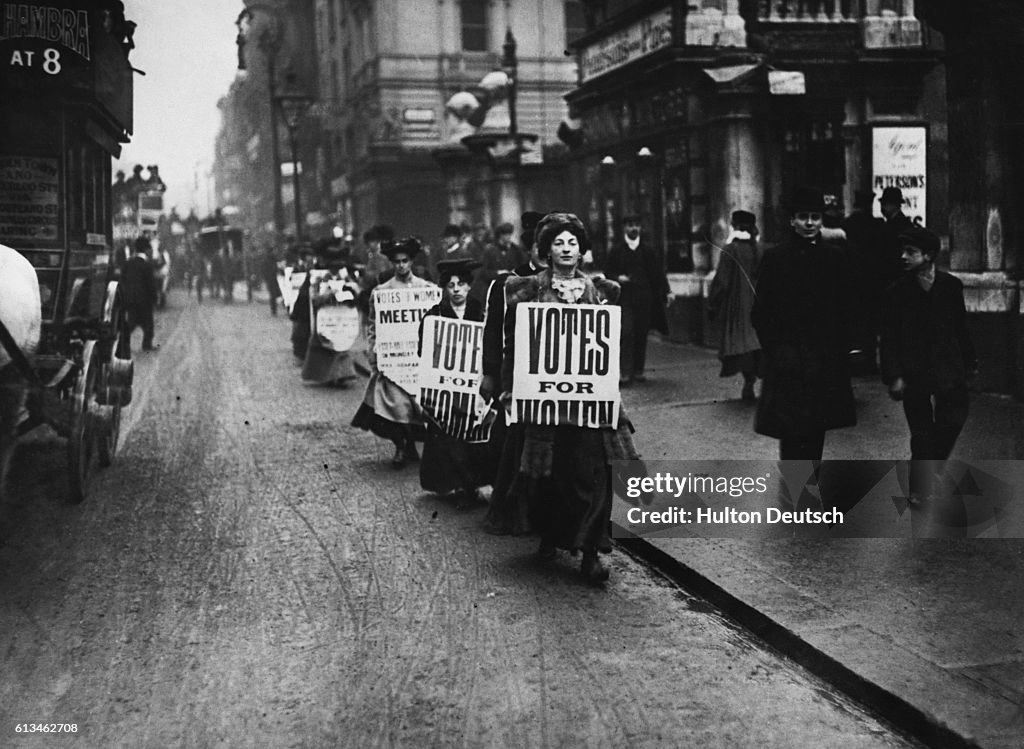 A line of placard holding Suffragettes walk down a London street ... A line of placard holding Suffragettes walk down a London street ...