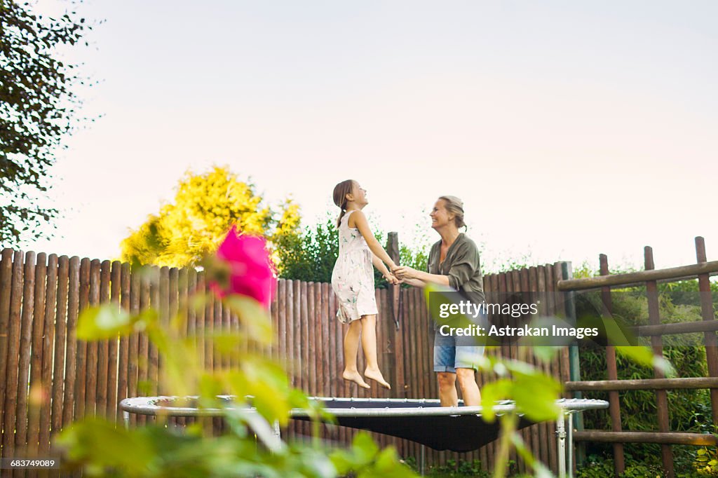 Mother And Daughter Jumping On Trampoline In Garden High Res Stock
