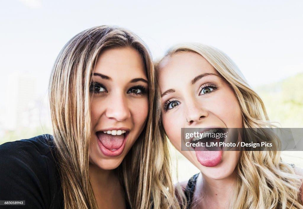 Two Girlfriends Posing For The Camera And Making Funny Faces In A Downtown City Park High Res