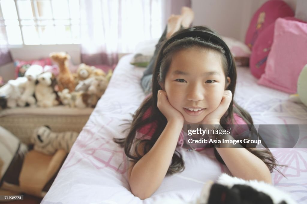 Girl In Bedroom Lying On Bed Hands On Chin Looking At Camera High Res