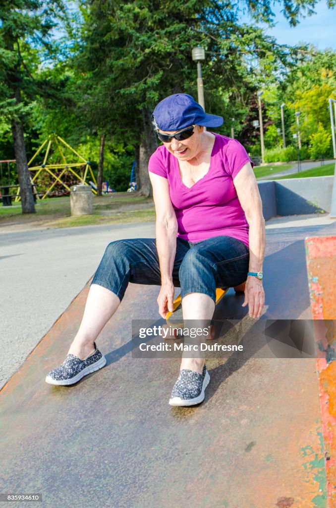 Senior Woman Wearing Baseball Cap On The Side And Sitting On Skateboard