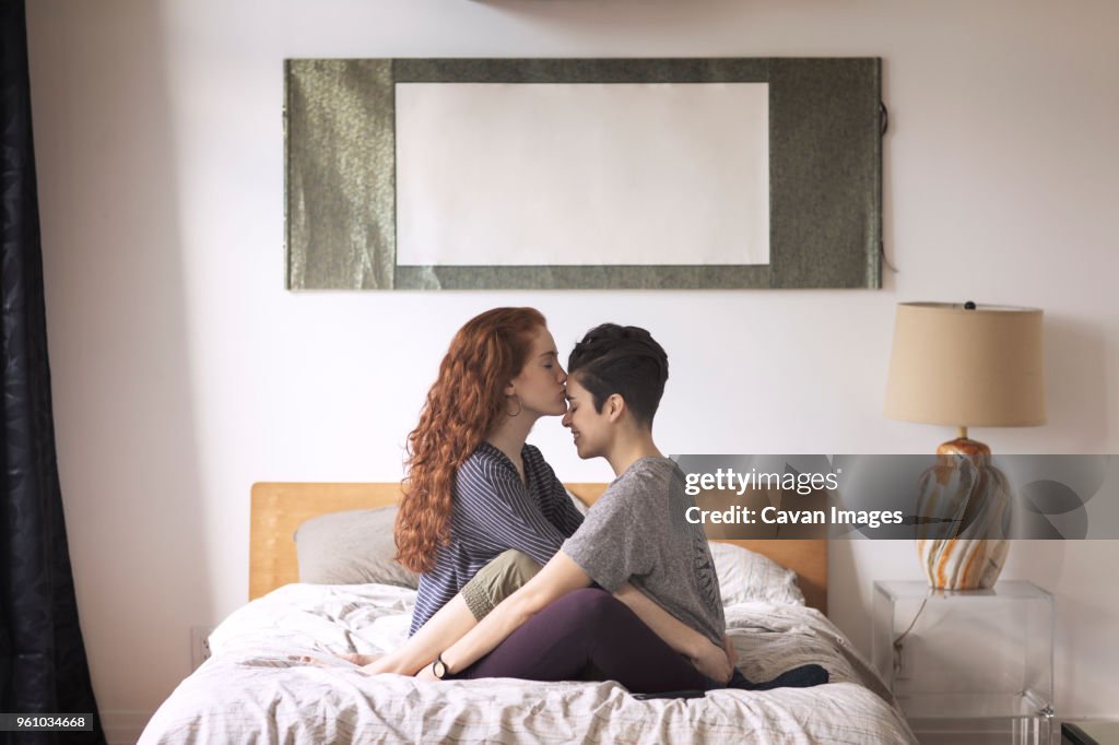 Romantic Lesbian Kissing On Girlfriends Forehead While Sitting On Bed