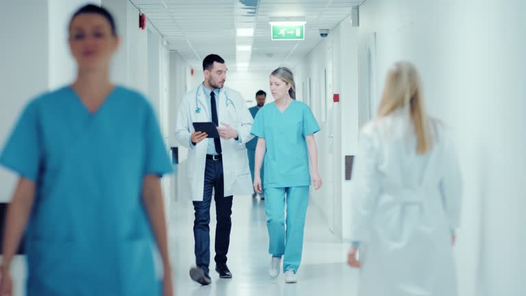 Surgeon And Female Doctor Walk Through Hospital Hallway They Consult