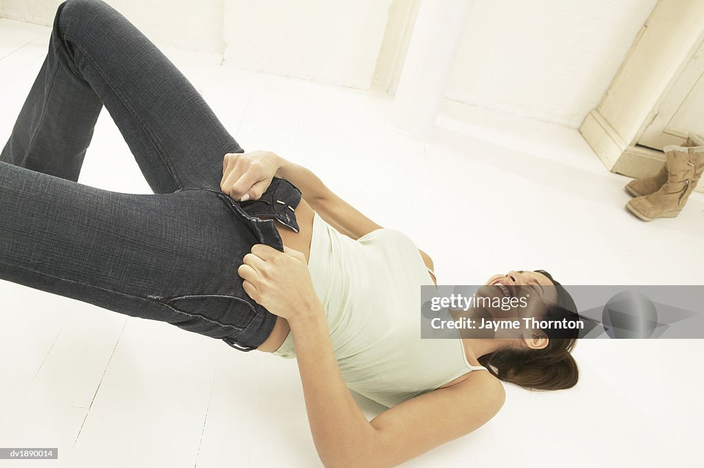 Woman Lying On Wooden Floor Trying To Fit Into Jeans High Res Stock